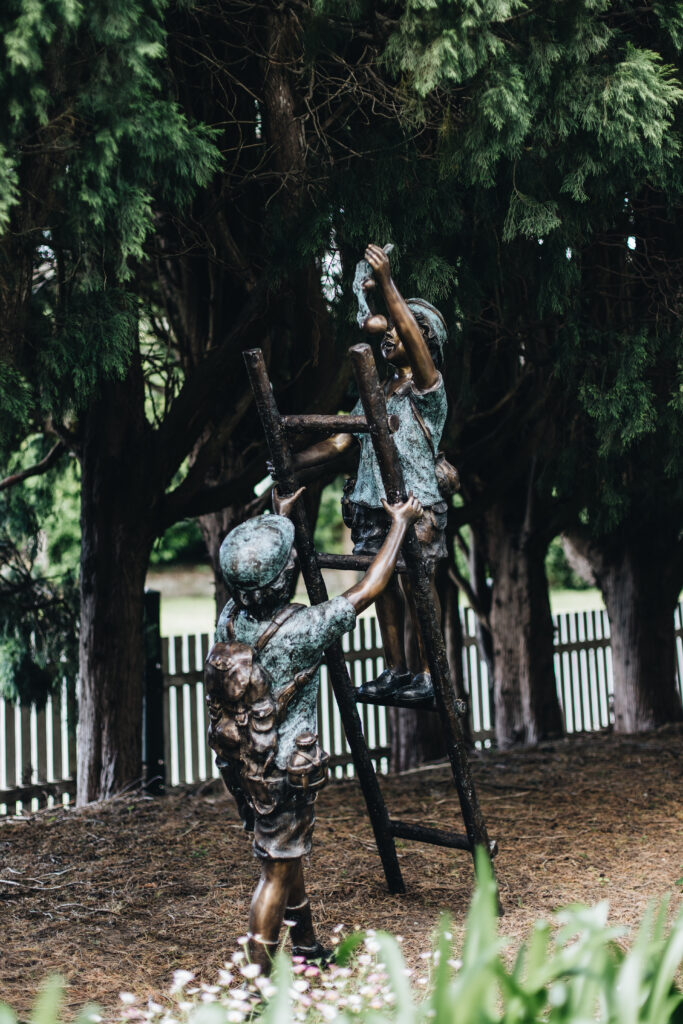 A bronze statue of two boys climbing a ladder - The Old Pot Factory